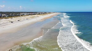 Uma praia com uma extensa faixa de areia, algumas pessoas e céu claro.