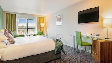 Quarto de hotel com cama, escrivaninha, cadeira, televisão e vista para a cidade.