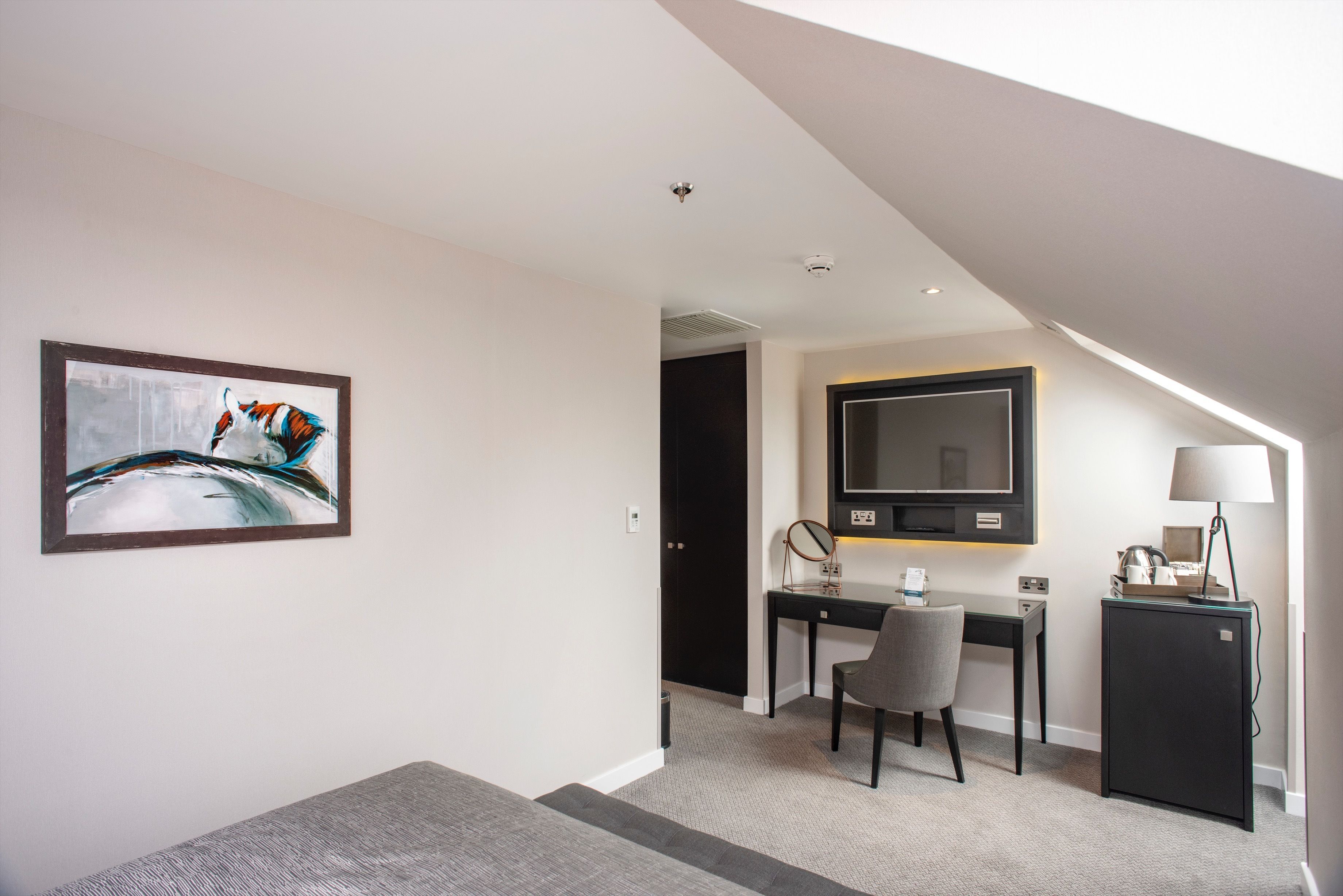 Quarto de hotel moderno com escrivaninha, cadeira e televisão de tela plana fixada na parede.