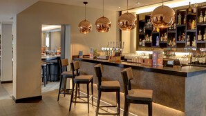 Uma área de bar com balcão, banquetas e uma estante de bebidas bem abastecida.