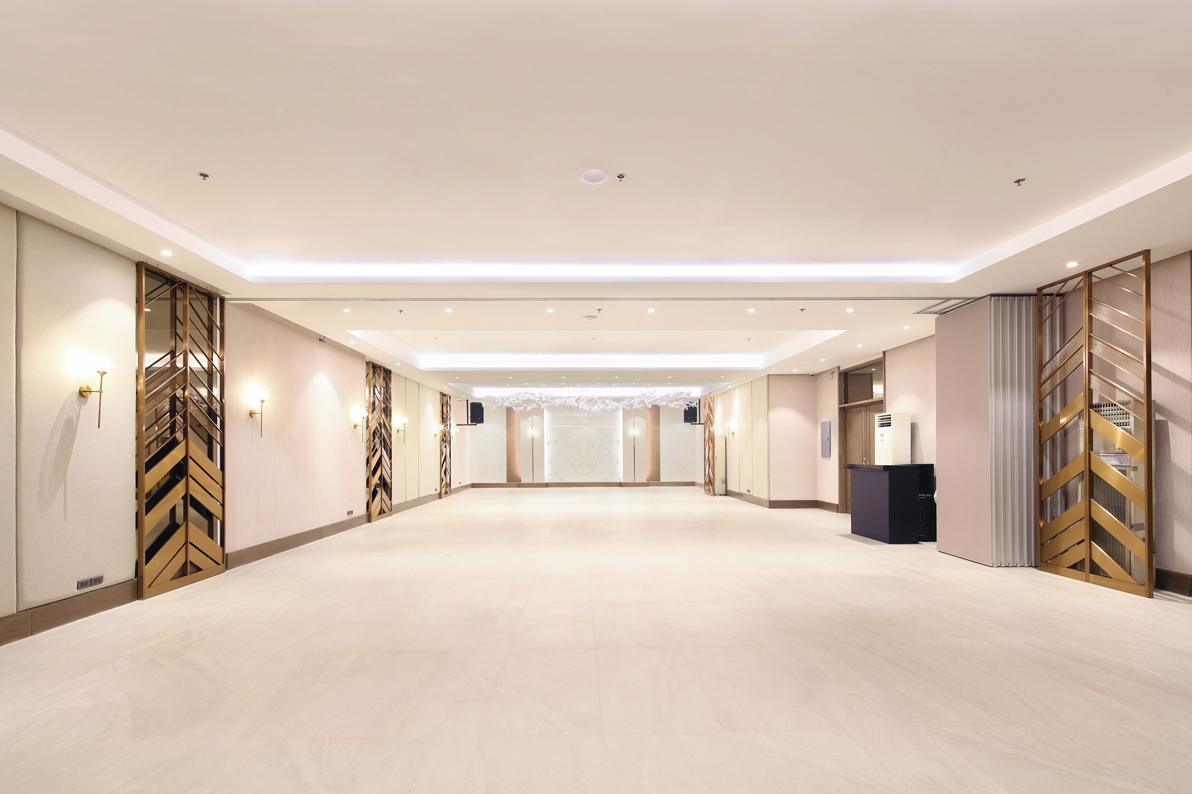 Um corredor de hotel espaçoso com design moderno, apresentando um layout amplo e aberto, com um candelabro central e um pódio em uma extremidade.