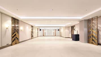 Um corredor de hotel espaçoso com design moderno, apresentando um layout amplo e aberto, com um candelabro central e um pódio em uma extremidade.