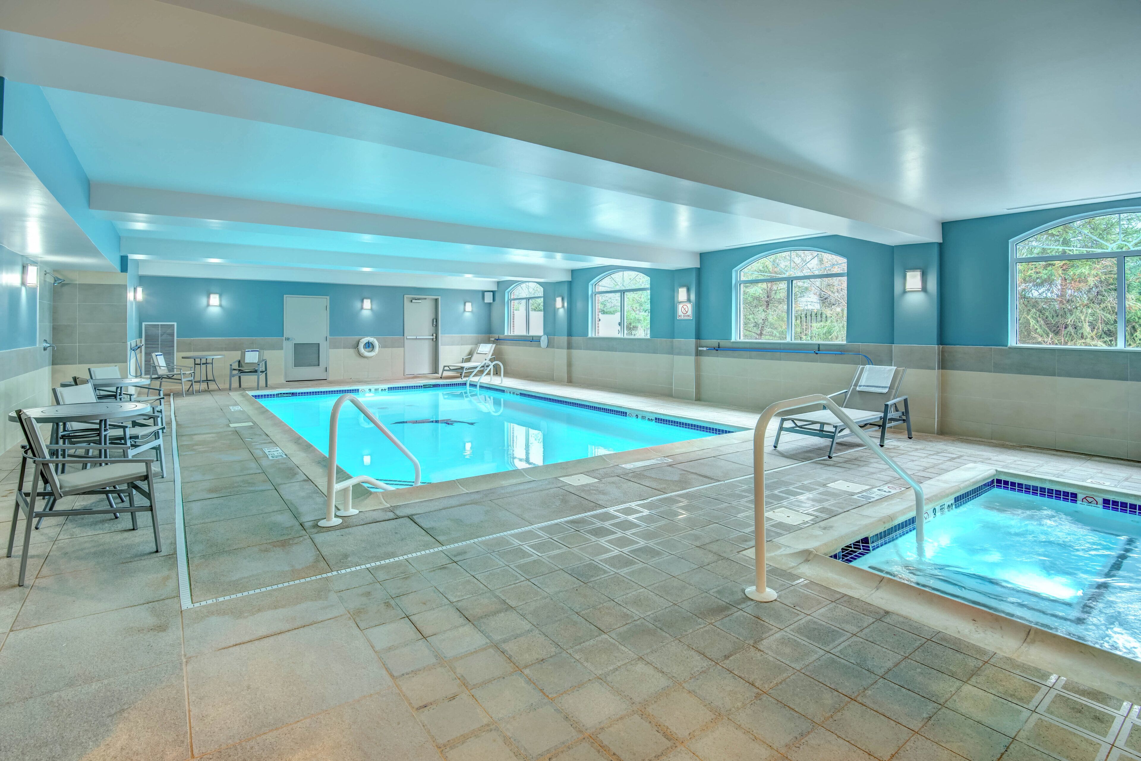 Uma área de piscina com piso ladrilhado, espreguiçadeiras e um espaço de estar pequeno com mesas.