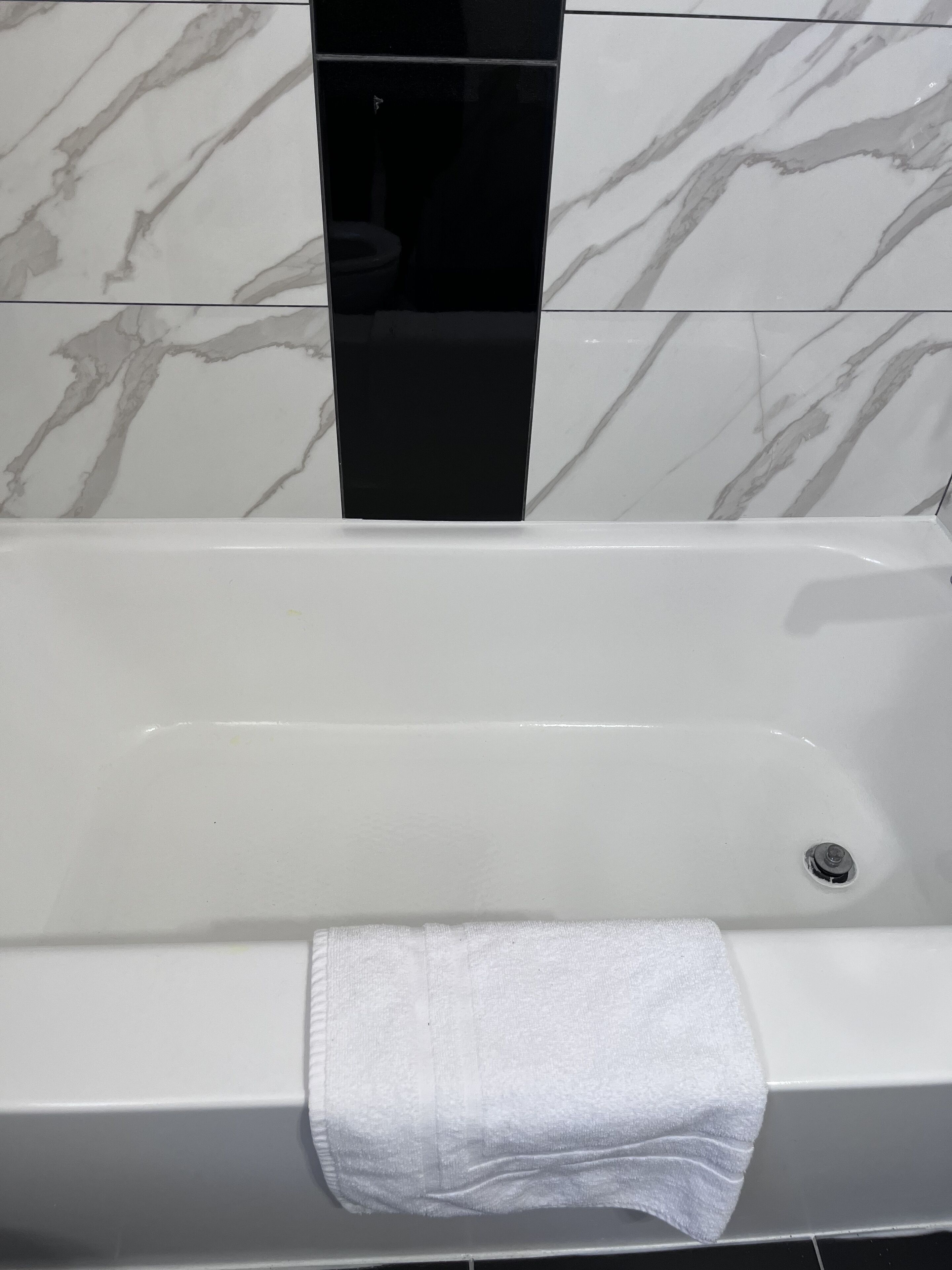 Um banheiro com uma banheira branca, um objeto vertical preto na parede e um revestimento de parede com padrão de mármore.