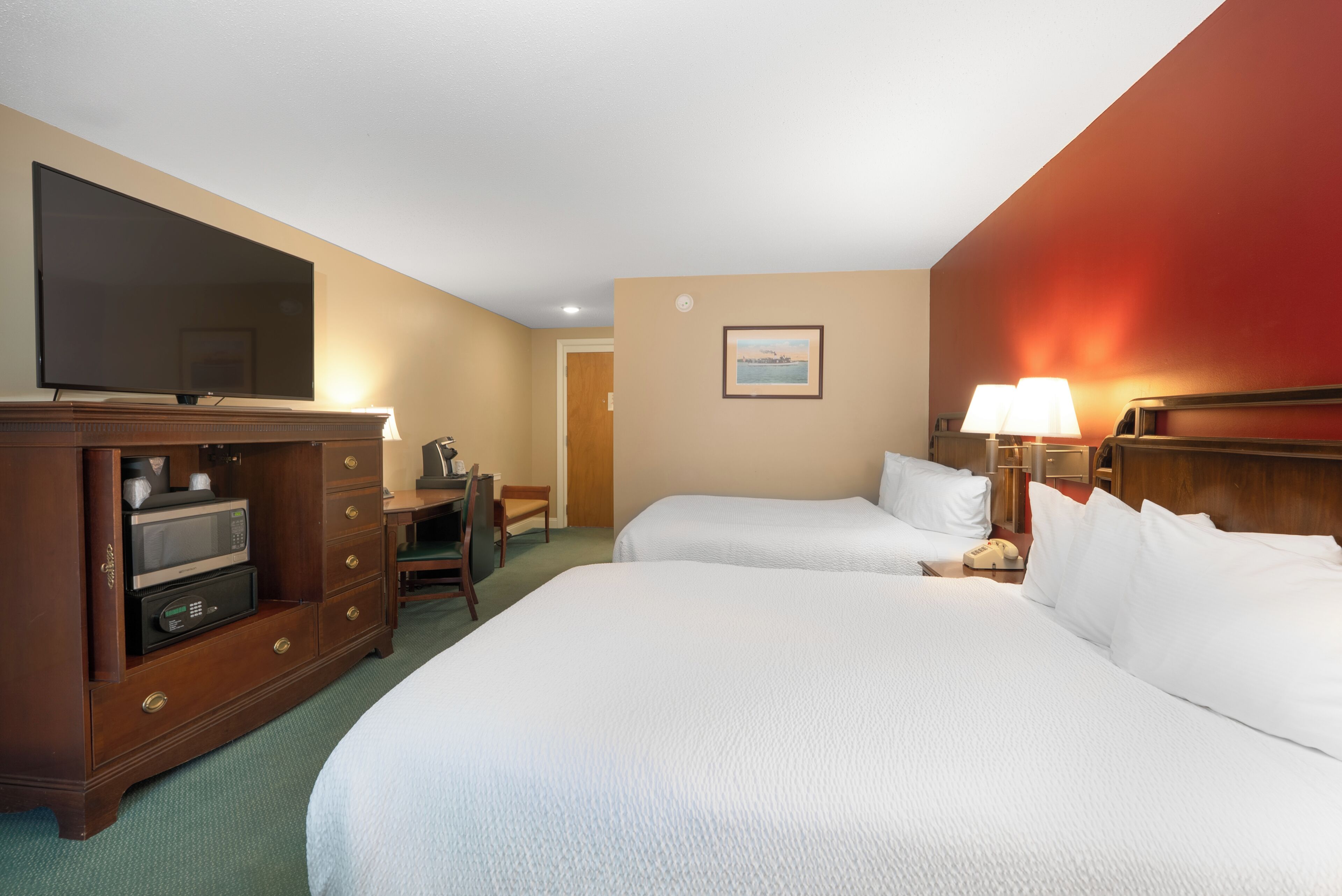 Quarto de hotel com duas camas, televisão, secretária com cadeira, micro-ondas e uma lâmpada.