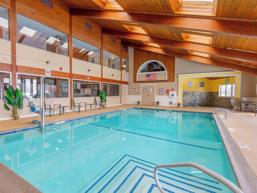 Piscina interna com vigas de madeira, parede de pedra e vista para o andar superior.