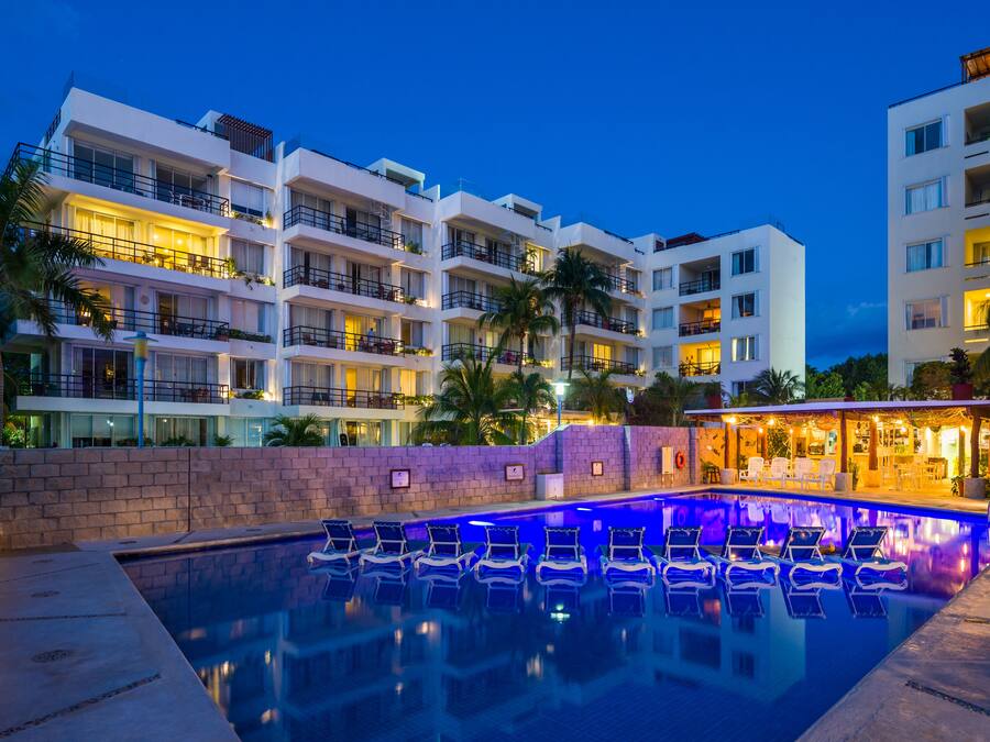 Um hotel com várias varandas, uma piscina com espreguiçadeiras e um espaço de bar.