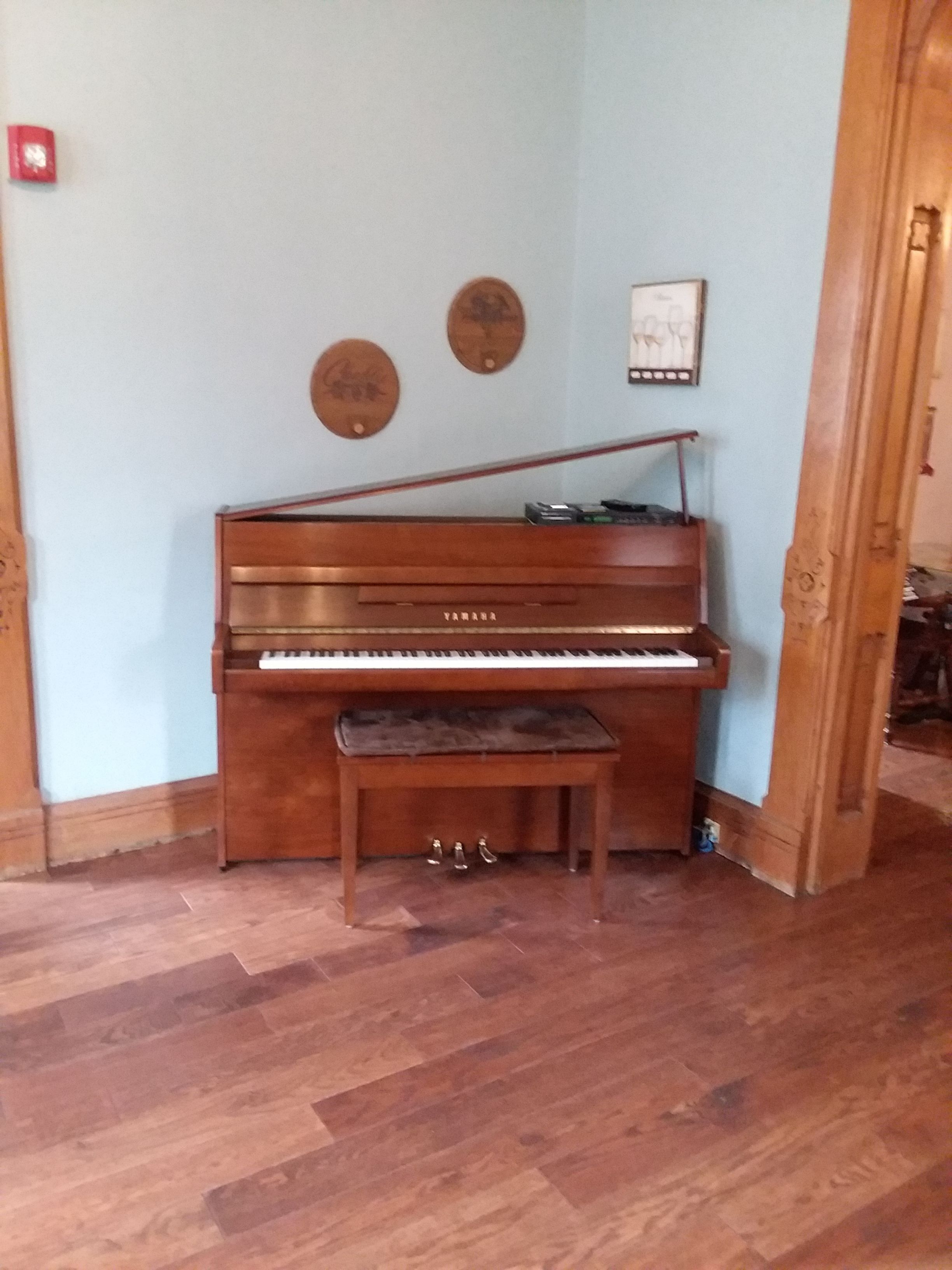 Um piano vertical Yamaha num quarto com paredes azul-claras e soalho de madeira.