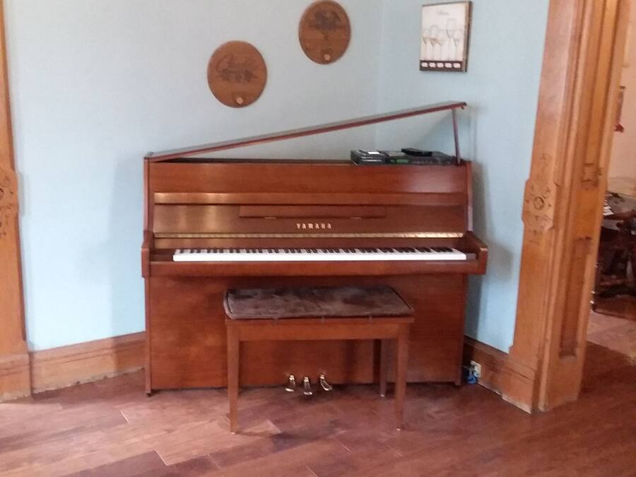 Um piano vertical Yamaha num quarto com paredes azul-claras e soalho de madeira.