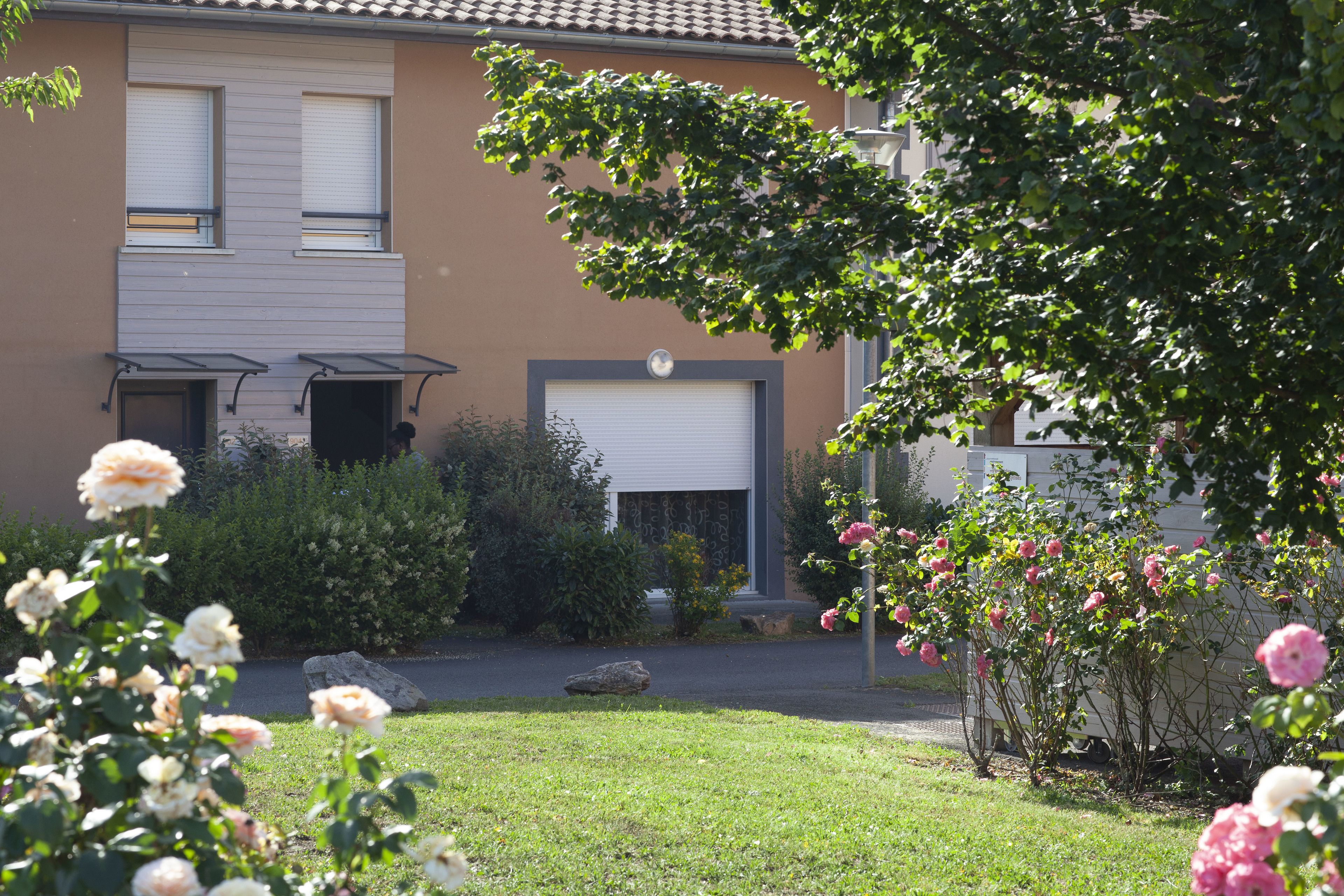 Um edifício residencial com porta de garagem, gramado com flores e uma árvore.