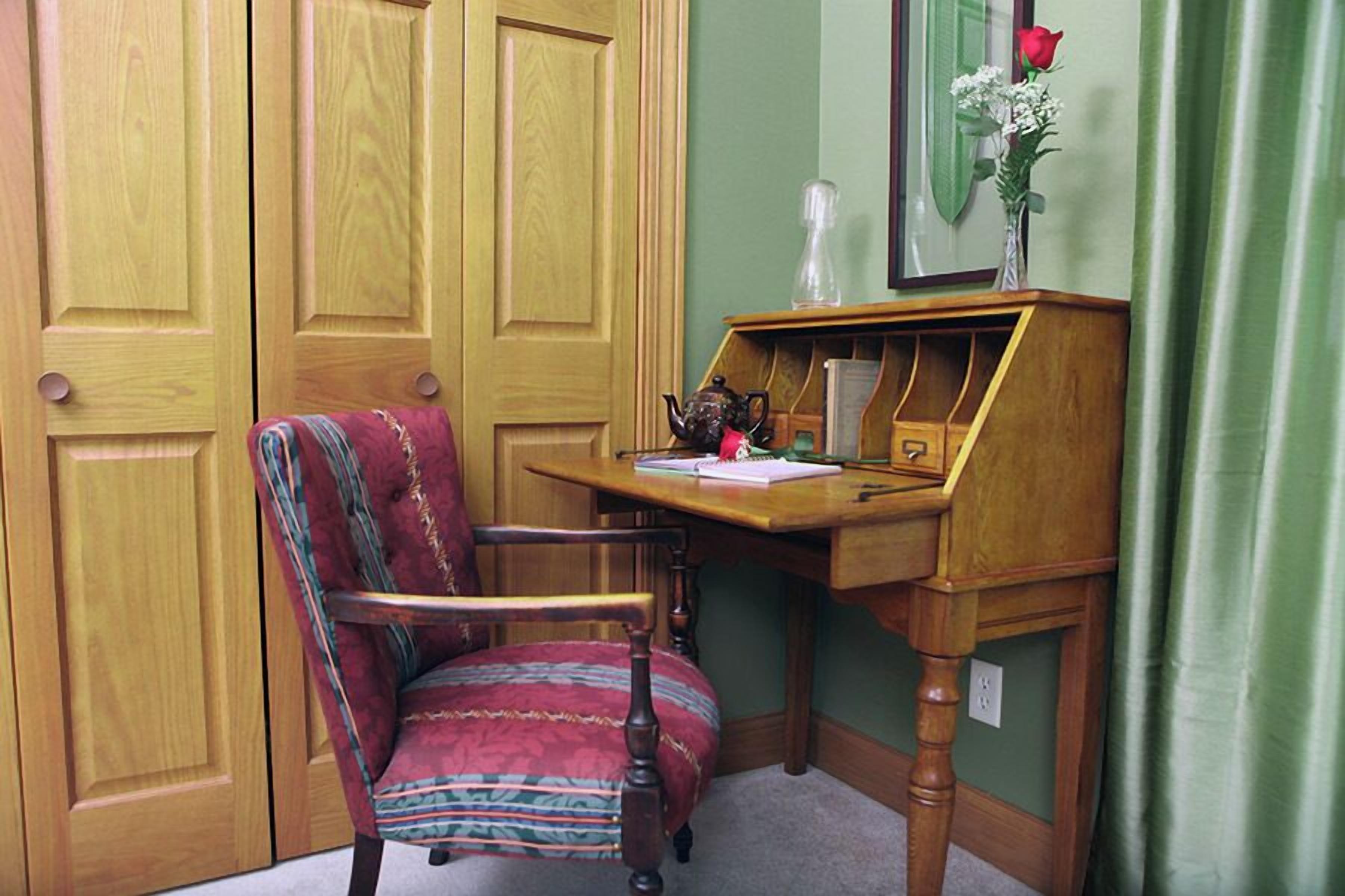 Quarto de canto com escrivaninha de madeira, poltrona estampada e cortina verde.