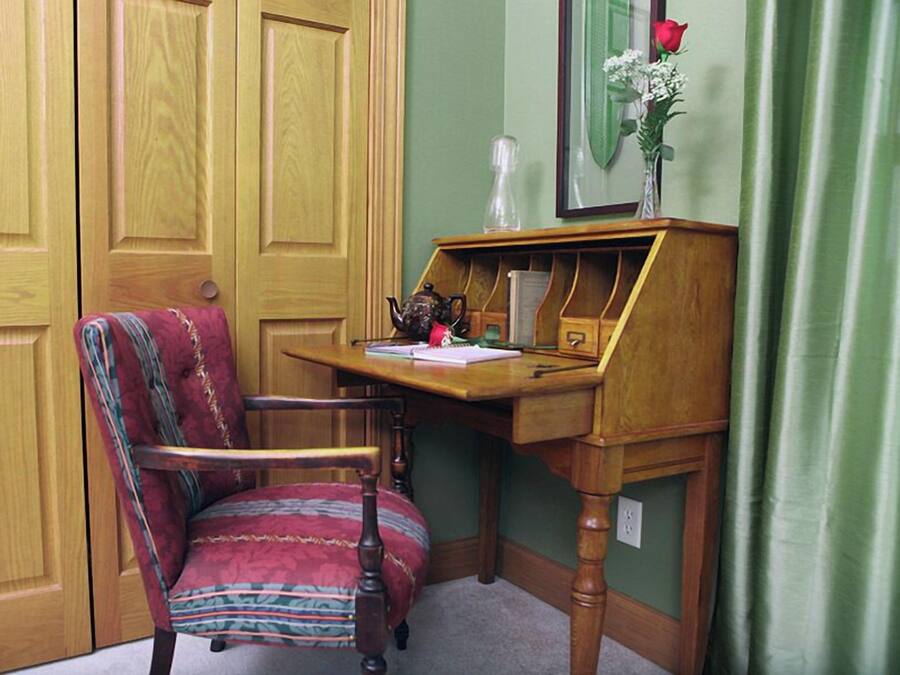 Quarto de canto com escrivaninha de madeira, poltrona estampada e cortina verde.