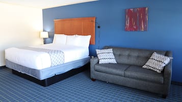 Quarto de hotel com uma cama, um sofá cinza, parede azul e um quadro abstrato vermelho.
