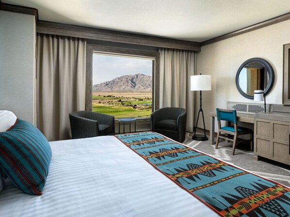 Quarto de hotel com uma cama grande, uma escrivaninha, uma cadeira, um abajur e vista para uma paisagem montanhosa.
