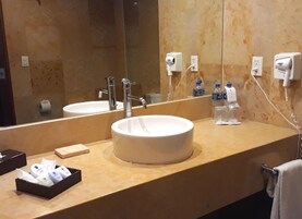 Uma casa de banho com uma pia redonda, um espelho e um porta-toalhas. Há artigos de higiene pessoal e um saboneteiro no balcão.