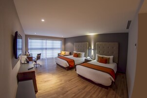 Quarto de hotel moderno com duas camas, uma escrivaninha, uma cadeira e uma janela grande.