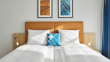Cama bem arrumada com lençóis brancos, um travesseiro azul e duas molduras na parede.