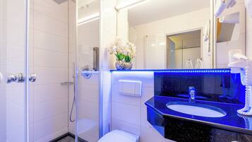 Uma casa de banho moderna com cabine de duche em vidro, lavatório preto com iluminação LED azul e sanita branca.