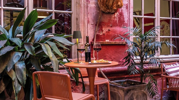 Uma área de pátio com mesa, cadeiras, plantas em vasos e um muro decorativo.