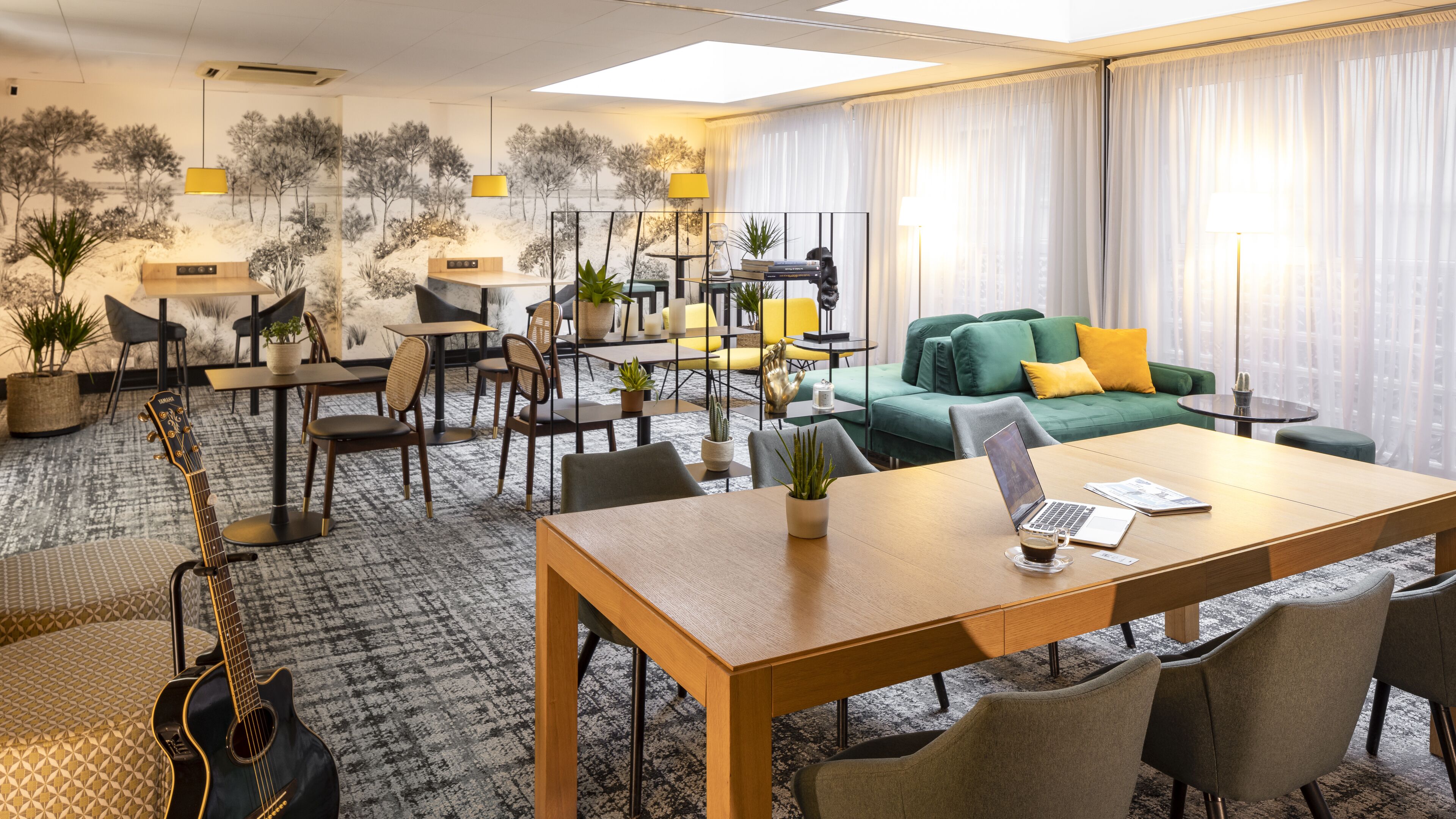 Quarto de hotel moderno com área de jantar, sofá verde e uma guitarra.