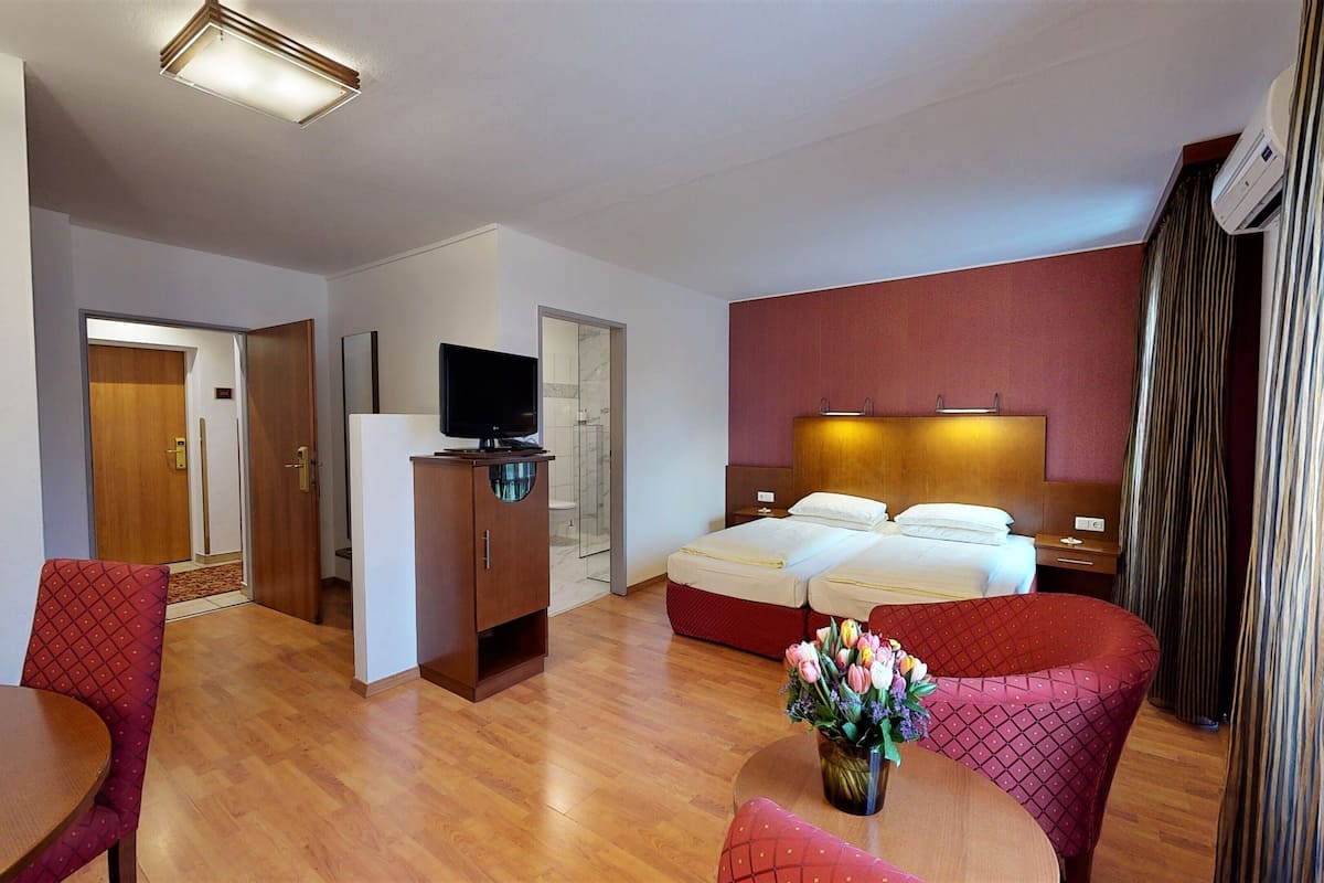 Quarto de hotel com cama, televisão, escrivaninha e cadeira.