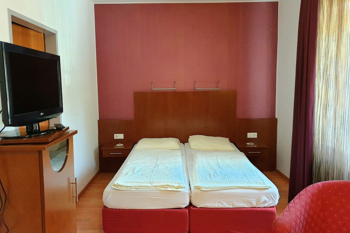 Quarto de hotel com duas camas, uma televisão e uma mesa de cabeceira de madeira.