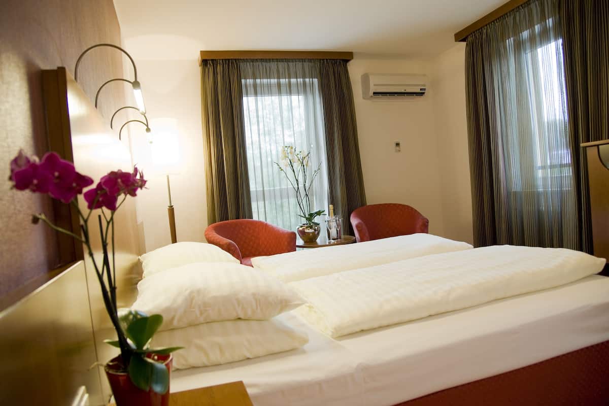 Quarto de hotel com cama, duas cadeiras, abajur e um vaso com flores.