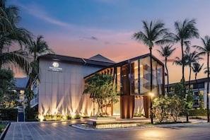 Um hotel moderno com uma placa de 'Doubletree' chamativa, entrada bem iluminada e área ajardinada com palmeiras.
