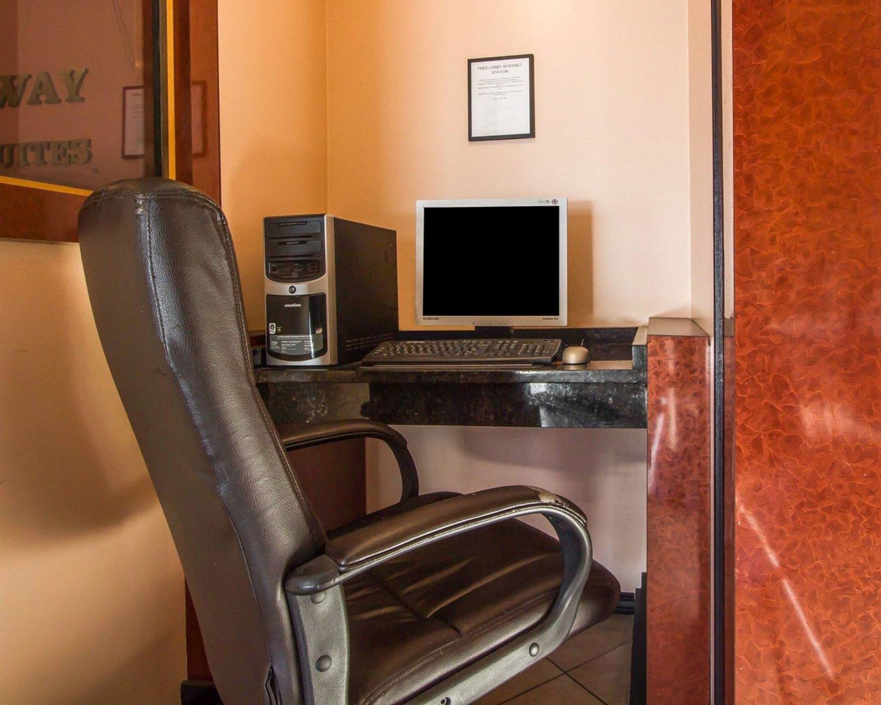 Uma mesa de escritório com um computador, um monitor e um teclado. Uma cadeira de couro preta está em frente à mesa.