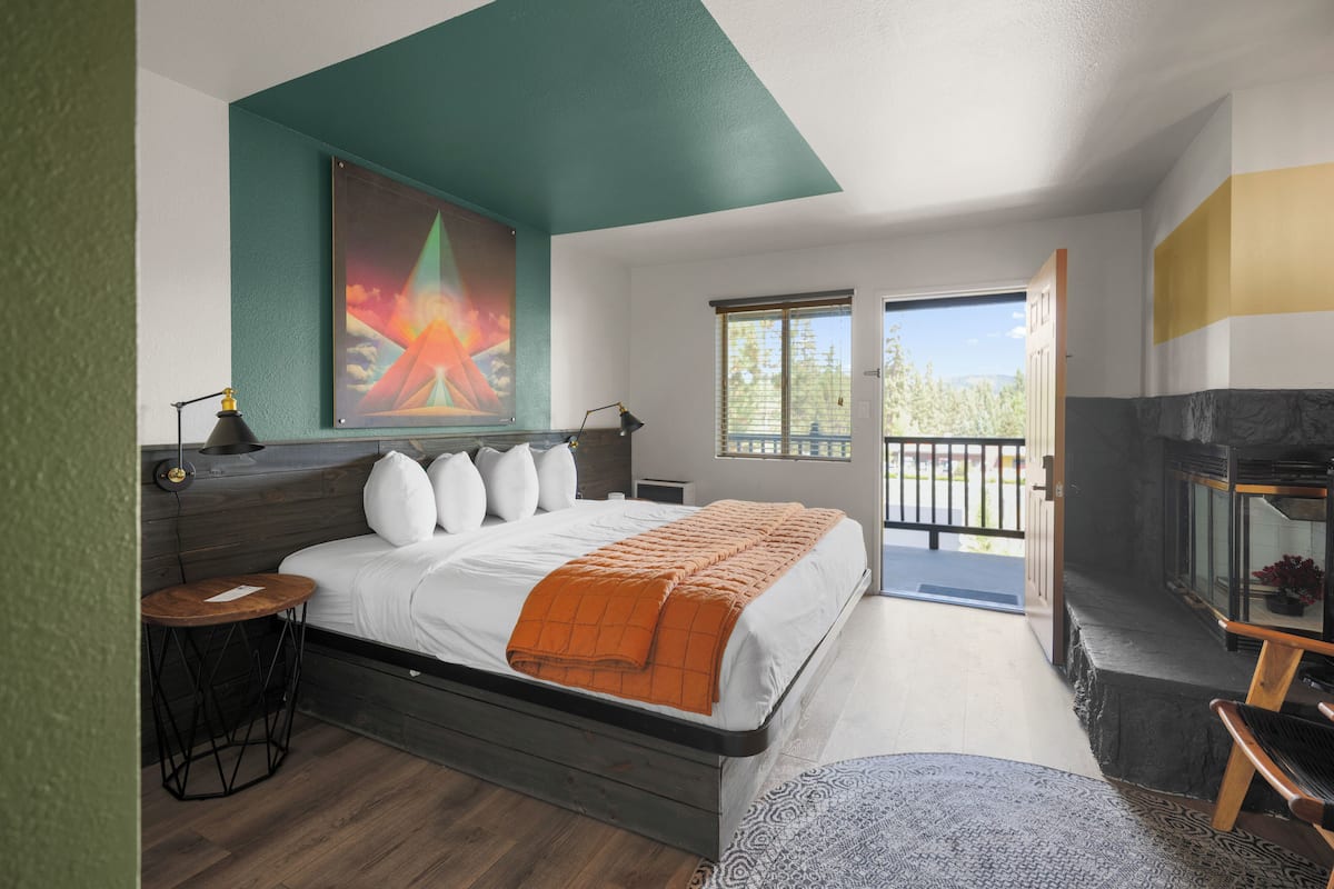 Quarto moderno com cama, mesinha, um quadro e lareira.