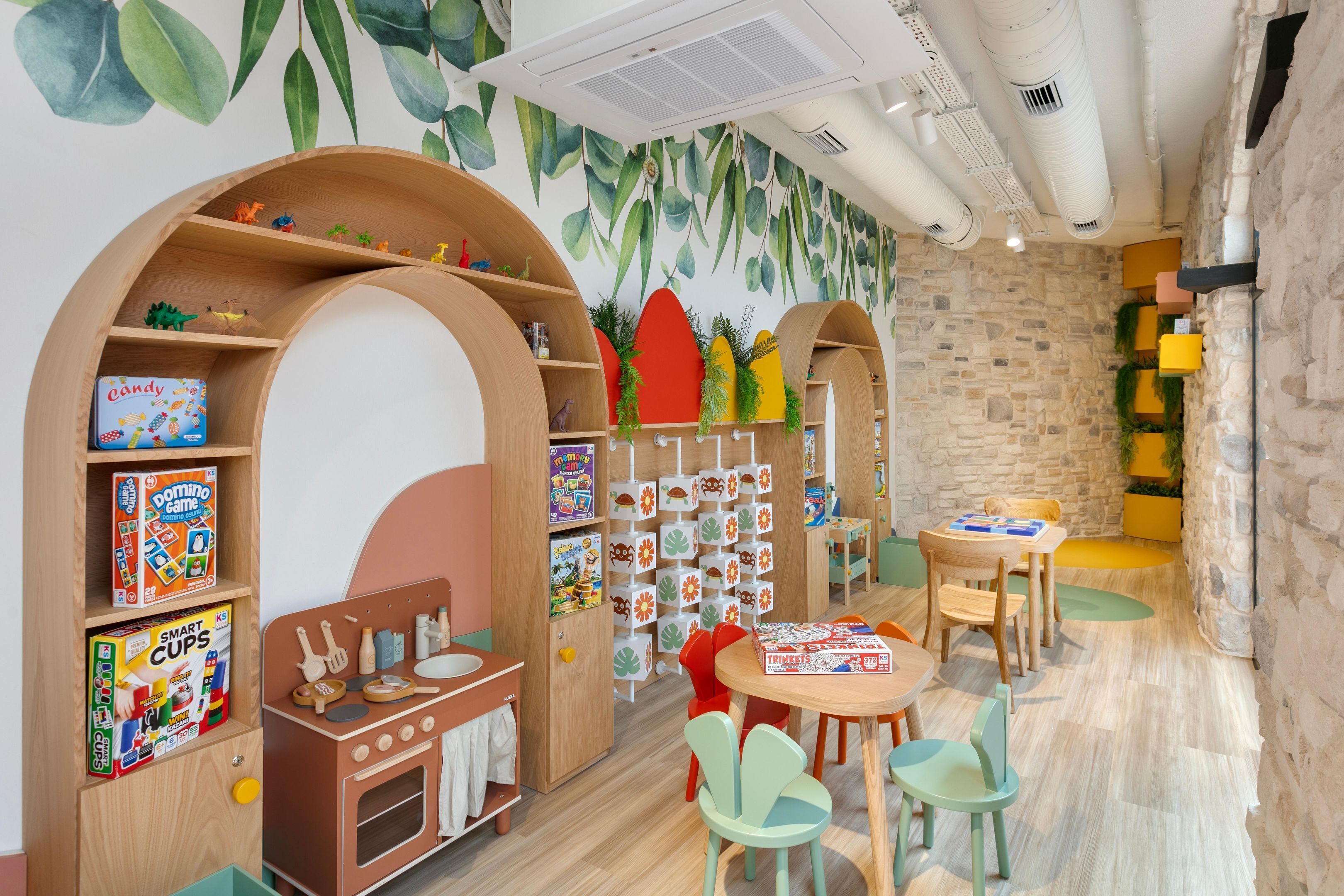 Espaço infantil com prateleiras de madeira, cozinha de brincar e cadeiras coloridas.