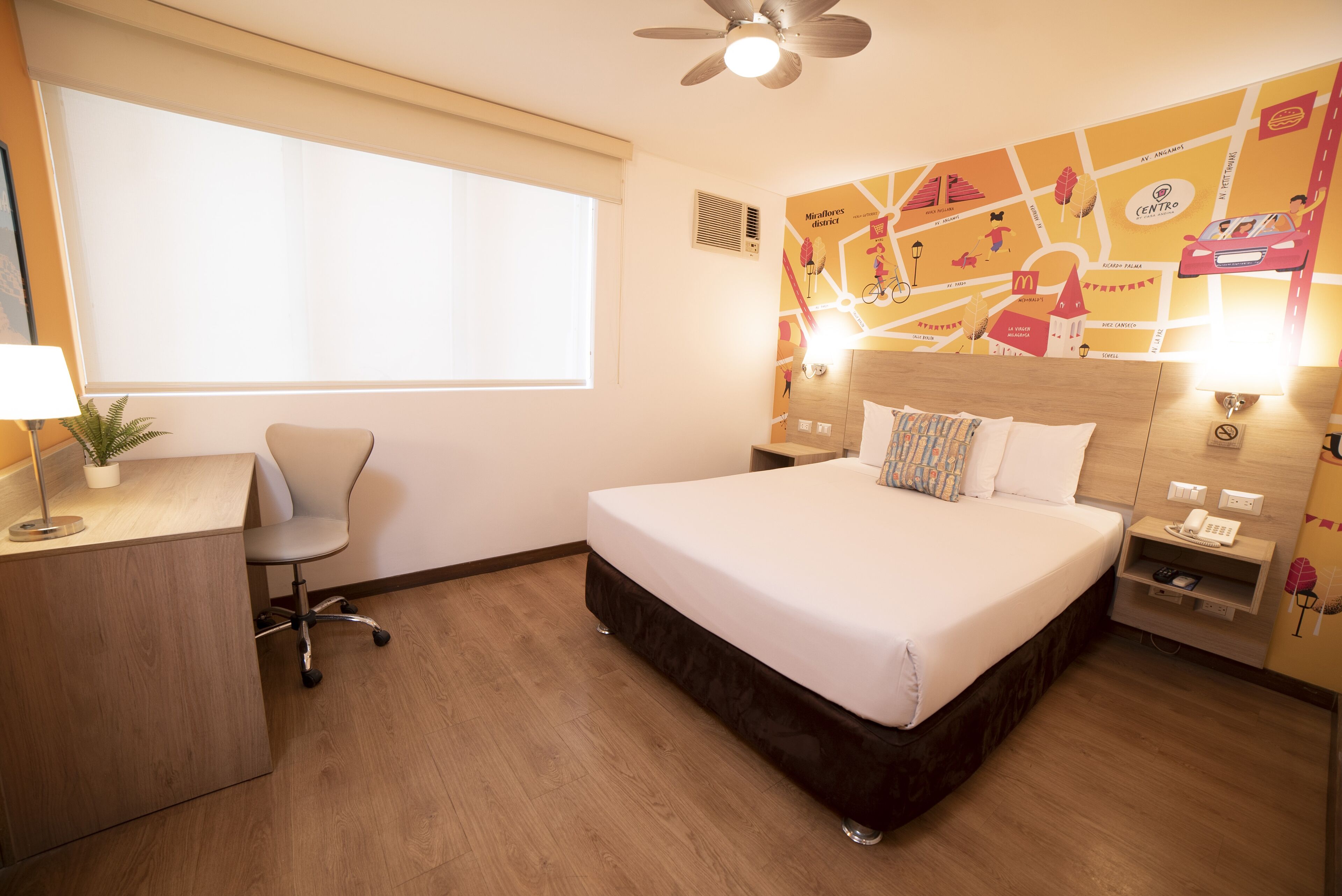 Quarto de hotel com cama, escrivaninha, cadeira e mapa na parede.