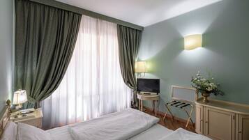 Quarto de hotel com duas camas, televisão, abajur, escrivaninha e um vaso de flores.