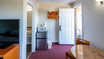 Quarto de hotel compacto com cozinha compacta, televisão, área de refeições com mesa e cadeiras, e piso coberto por um tapete vermelho.