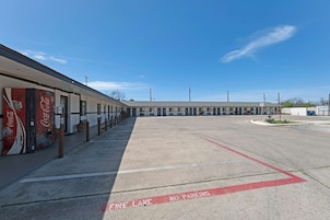 Uma faixa de acesso para emergências, sem estacionamento, uma máquina de refrigerantes Coca-Cola e uma fileira de quartos de motel.
