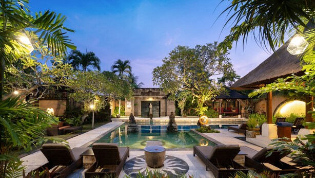Uma área ao lado da piscina com espreguiçadeiras, um elemento aquático central e vegetação ao redor.