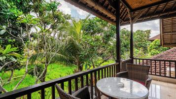 Varanda com móveis de vime, uma mesa redonda e vista para uma paisagem verdejante.
