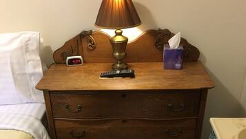 Uma mesa de cabeceira de madeira com uma luminária, um estojo de lenços de papel e um relógio digital mostrando 4:34.