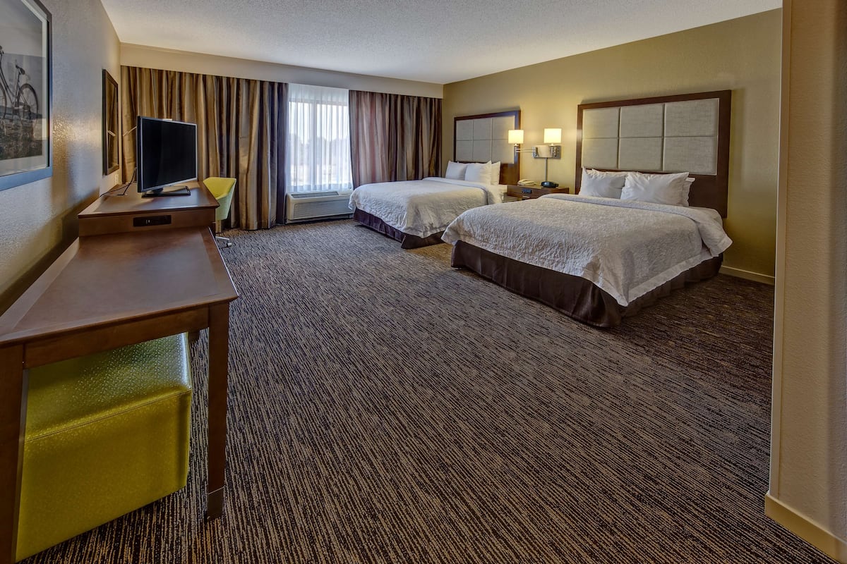 Quarto de hotel com duas camas, uma mesa, uma televisão e uma cadeira.
