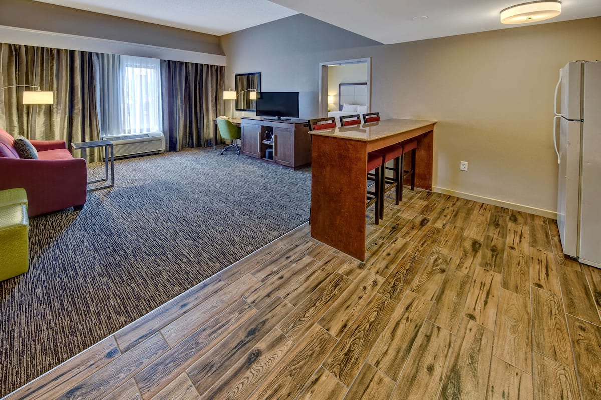 Quarto de hotel com chão de madeira, sofá vermelho, escrivaninha com cadeira, televisão e frigorífico.