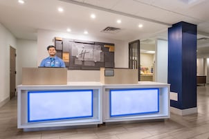 Uma receção de hotel com design moderno, com um ecrã digital e um balcão de madeira.