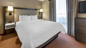 Quarto de hotel com cama grande, mesa de cabeceira, cômoda e televisão na parede.