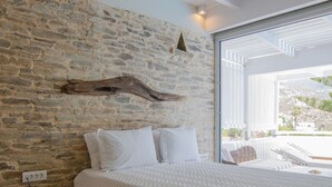Quarto com parede de pedra, cama com roupa de cama branca e vista para o exterior.