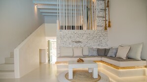 Uma sala de estar moderna com um sofá branco, uma pequena mesa de centro branca e um tapete texturizado. Uma escada com corrimão branco leva a um andar superior.