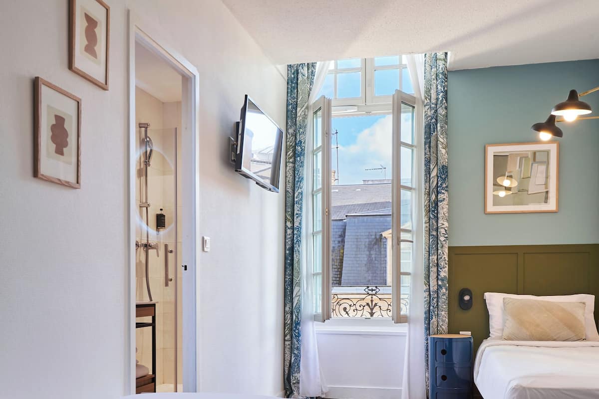 Quarto de hotel com duas camas, televisão na parede, janela com cortinas e vista para o exterior.