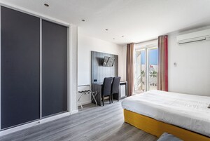 Quarto de hotel moderno com cama, escrivaninha, cadeiras e porta deslizante.