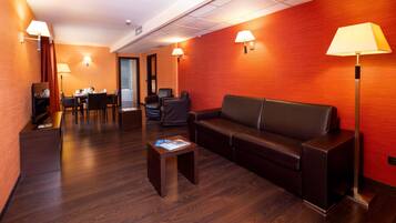 Um hall de hotel com um sofá de couro marrom escuro, uma mesa de centro de madeira e uma área de refeições com mesa e cadeiras.
