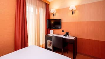 Quarto de hotel com cama, escrivaninha, televisão e minibar.