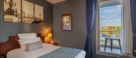 Quarto de hotel com uma cama grande, vista para uma varanda e um quadro na parede.