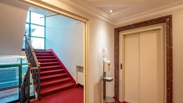 Uma escadaria com carpete vermelho que leva a um quarto com porta branca e moldura de mármore.